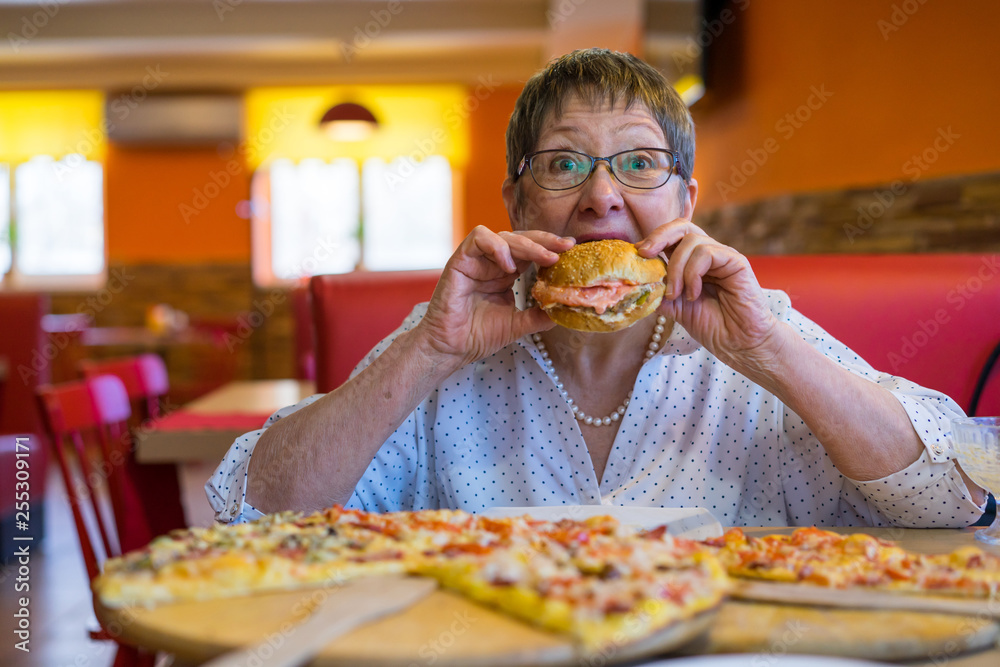 Hungry mature woman eagerly and violently eats fast food. Hamburger and ...