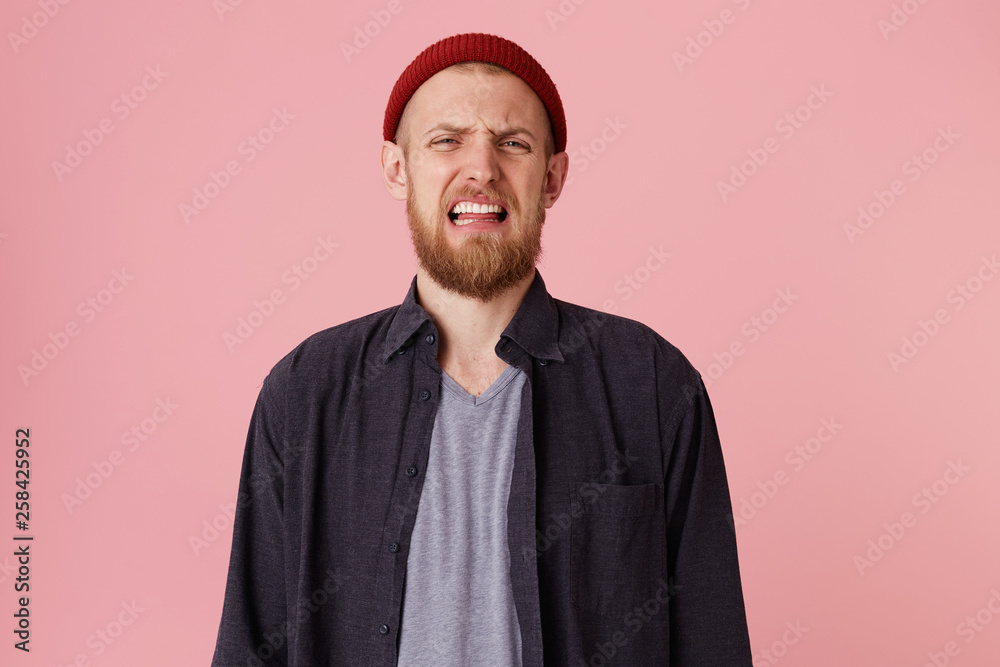 Ugh, how disgusting! Displeased young bearded male, with red hat, says ...