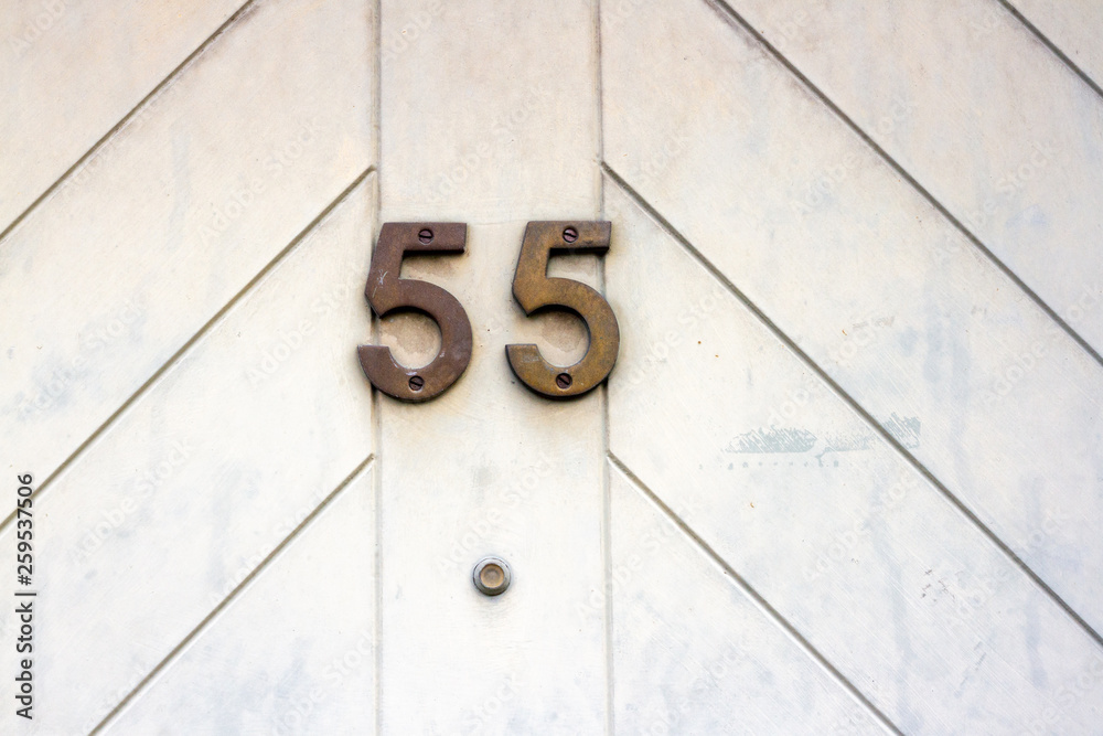 House number 55 with the fifty-five in bronze metal numbers on a wooden ...