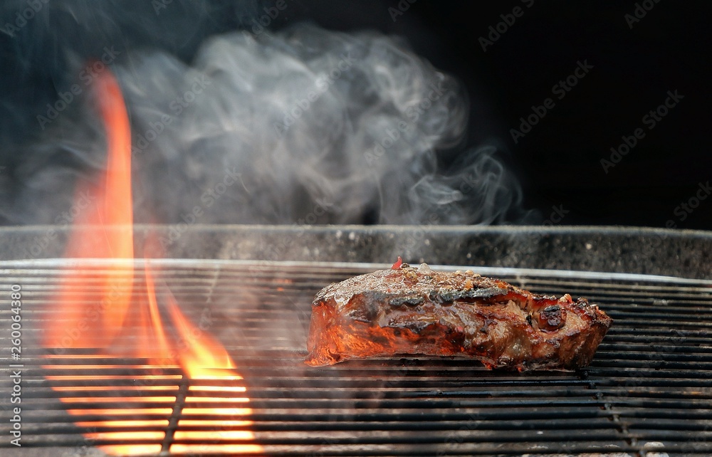 Roasted beef rip steak on flaming charcoal grill with fire flame and ...