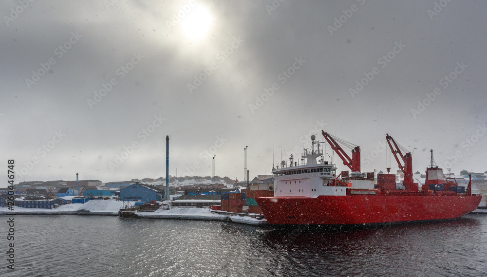 Big red cargo ship under the dull arctic sun and heavy snowfall in the ...