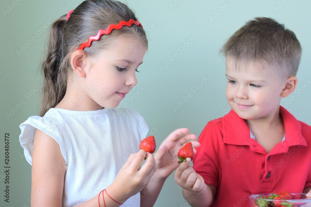 Two little Caucasian kids eat strawberries. Brother and sister eating ...