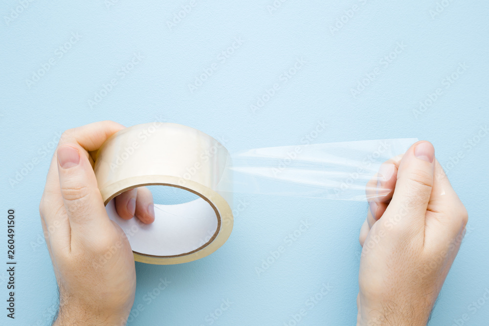 Man hands stretching transparent scotch. Light pastel blue background ...