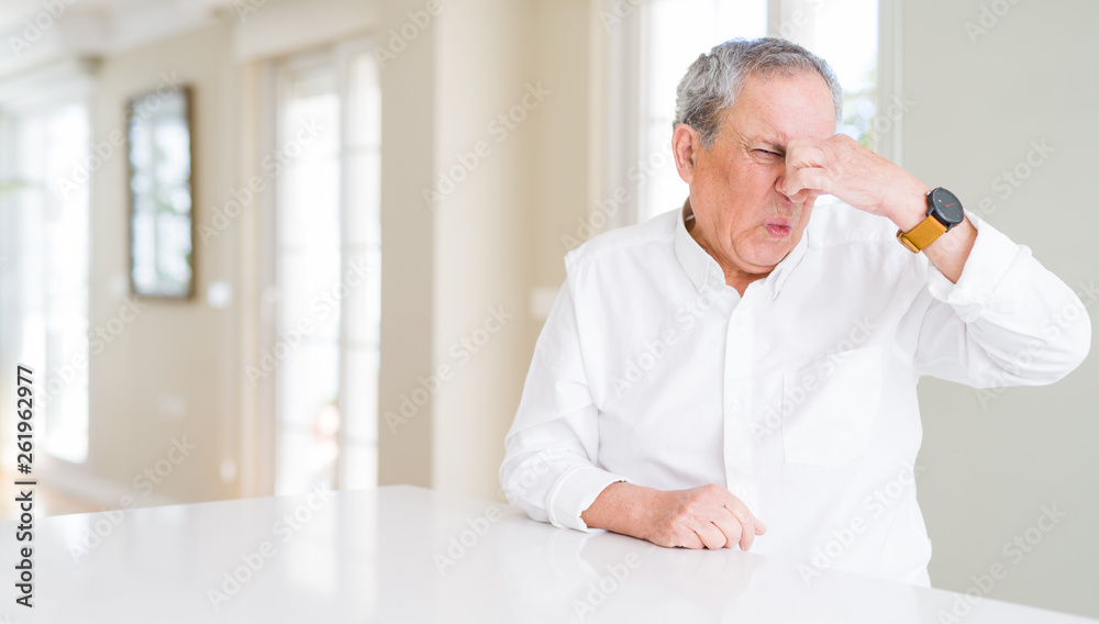 Handsome senior man at home smelling something stinky and disgusting ...
