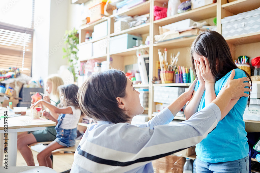 Side view of young female teacher comforting crying girl during lesson ...