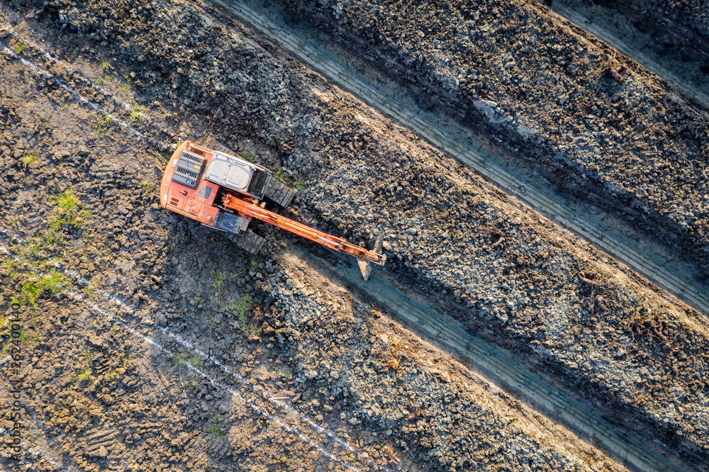 orange bachkhoe is digging soil creating grooves for planting parm and ...