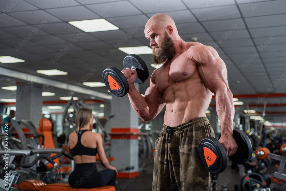 Brutal, muscular, bald with a beard athlete in the gym. Lifts heavy ...