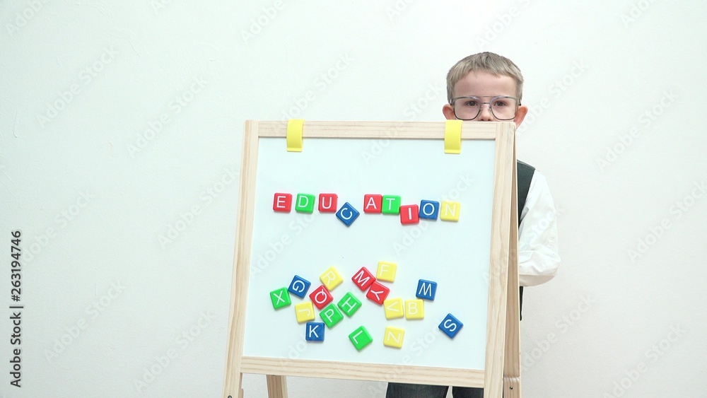 Amusing child with big eyeglasses writing behind whiteboard, happy kid ...