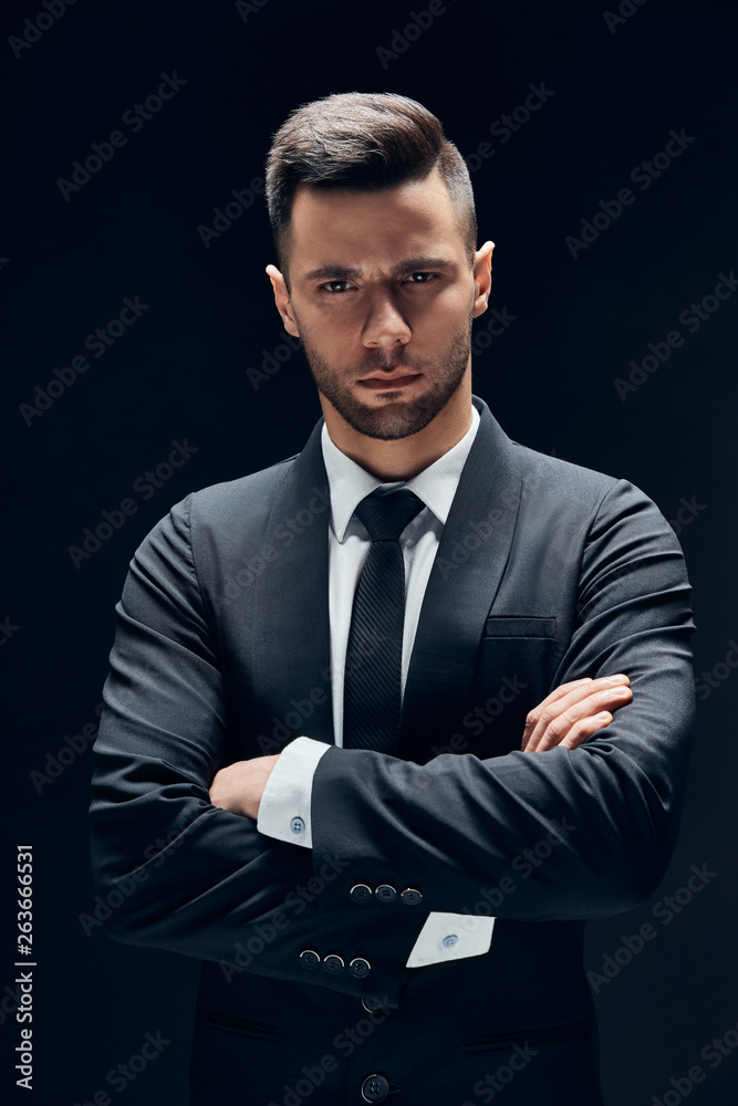 Handsome confident man in black suit with arms crossed on dark ...