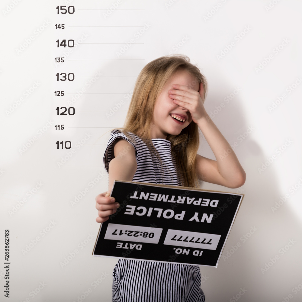 Young beautiful blonde child with a sign covers his face with his hand ...