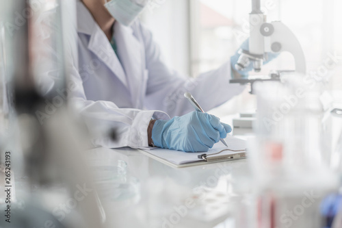 A scientist hands writing on a clipboard in laboratory with test tube ...