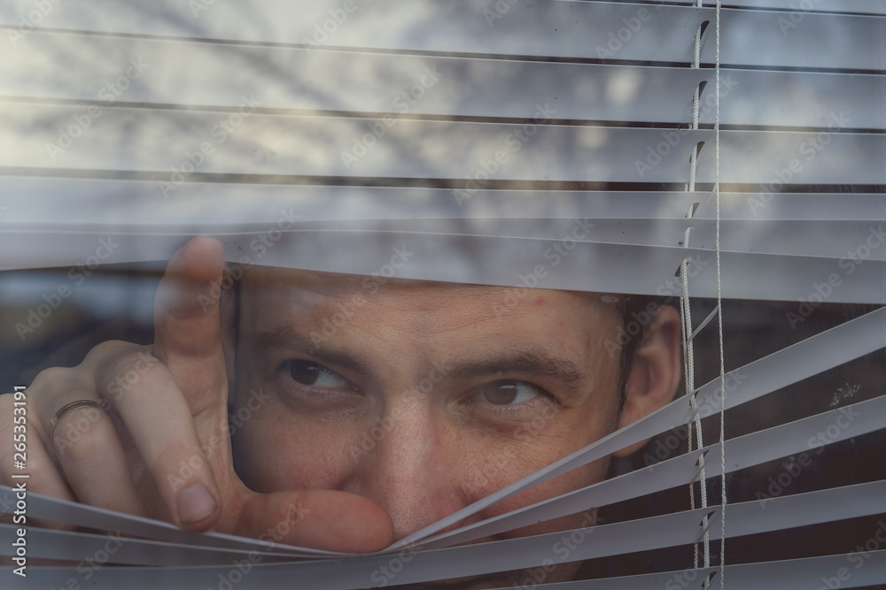 Man watching through window blinds Portrait of young thoughtful male ...