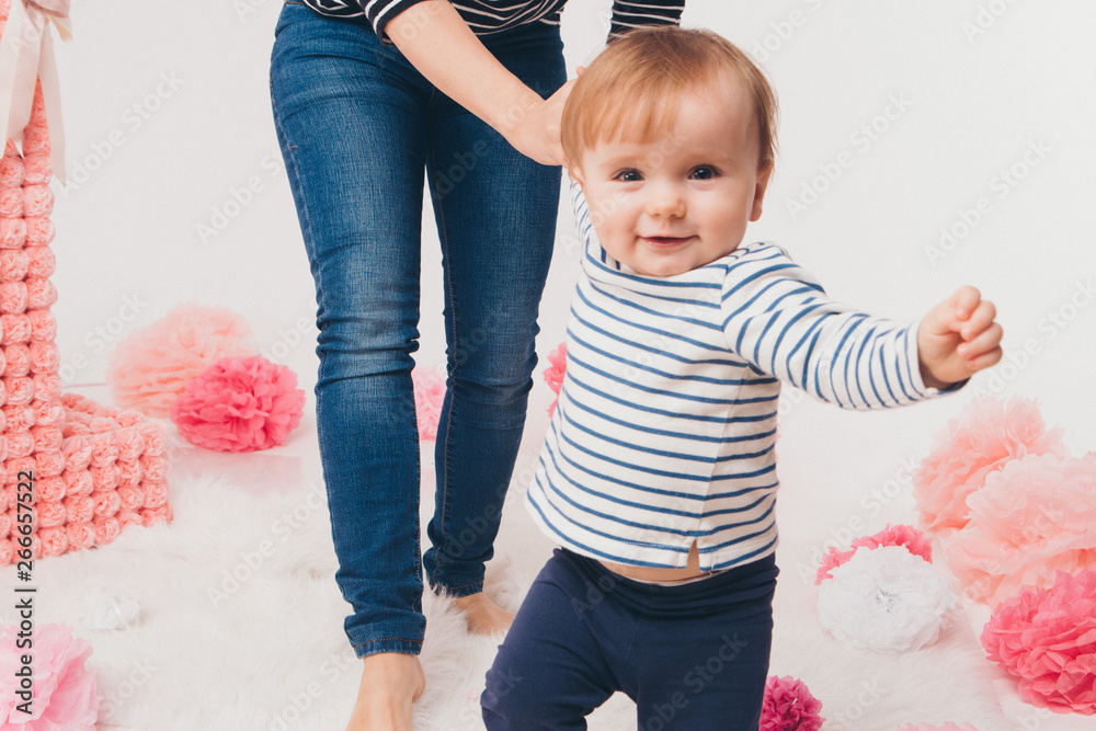 Cute baby learning to walk and make his first steps. mom is holding his ...