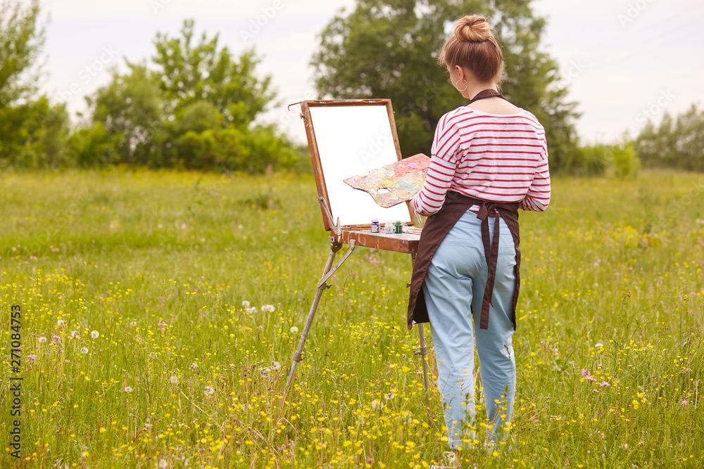Back view of young slim woman artist drawing picture on canvas in ...