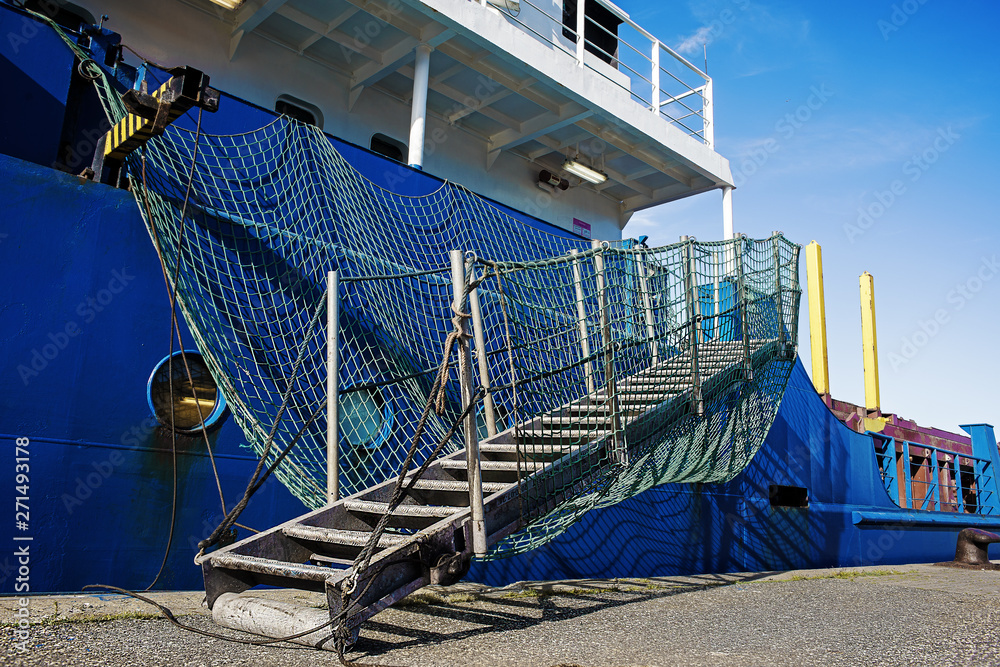 Stern of cargo vessel at port. Gangway arrangment. Blue hull. White ...
