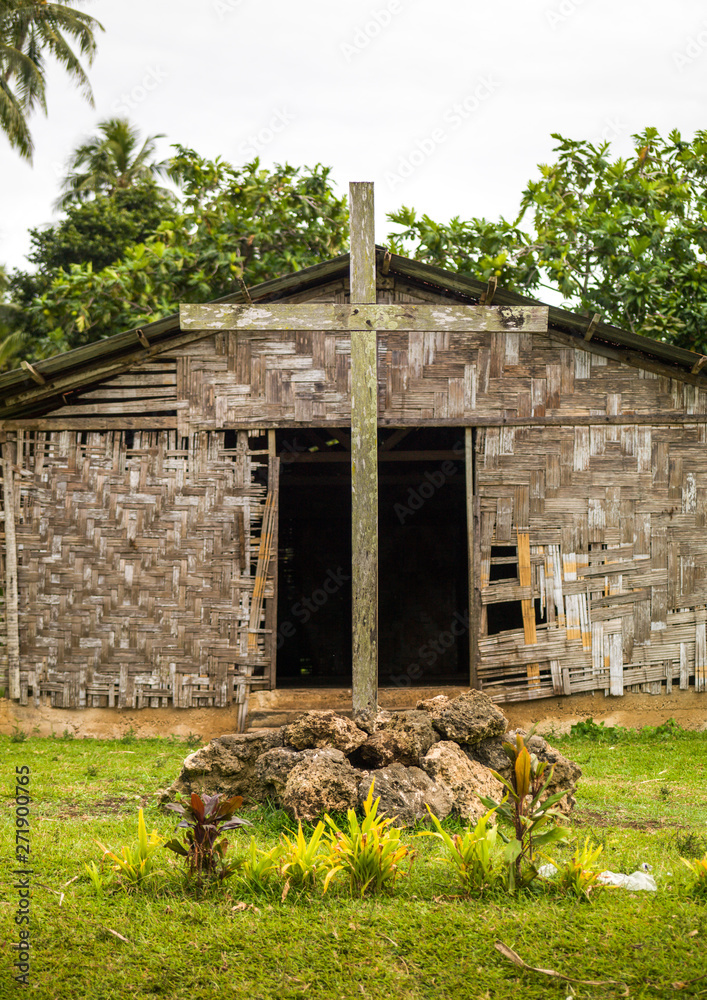 Tomb with a cross in front of a traditional house made with palm leaves ...