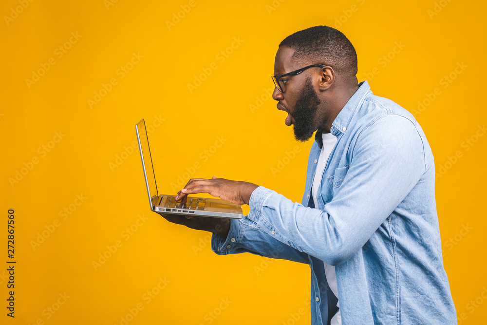 Young surprised african man standing and using laptop computer isolated ...
