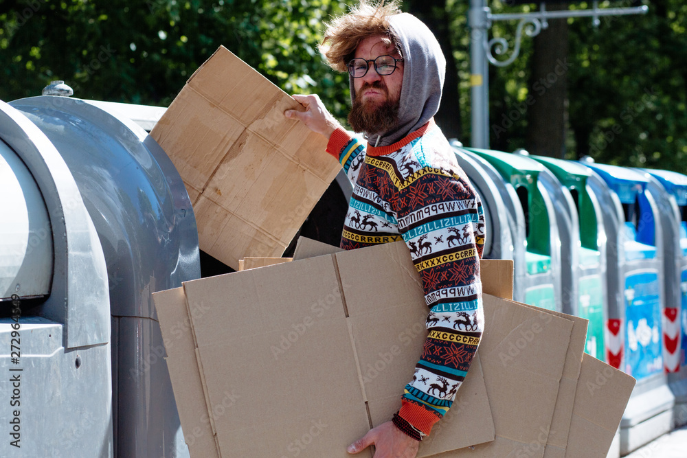 Homeless man collecting waste paper. Stylish beggar taking carton boxes ...