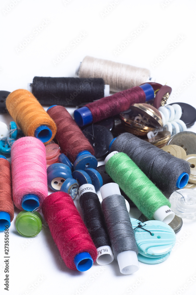 Colored spools of thread and buttons are a bunch on white background ...