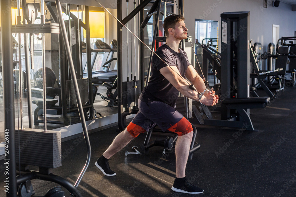 Side view of young adult confident crossfit man standing and doing trx ...