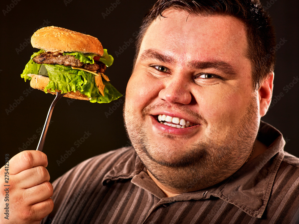 Fat man face eats burger on fork. Obeseness and overnutrition of fast ...
