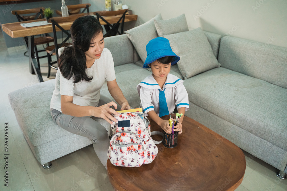 mom help her little girl preparing school stuff on her daughtes's ...
