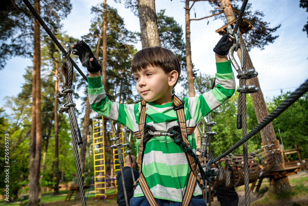 boy climbs in a high wire park above the ground. ziplining. boy on the ...