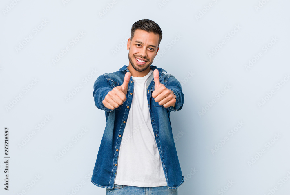 Young handsome filipino man with thumbs ups, cheers about something ...