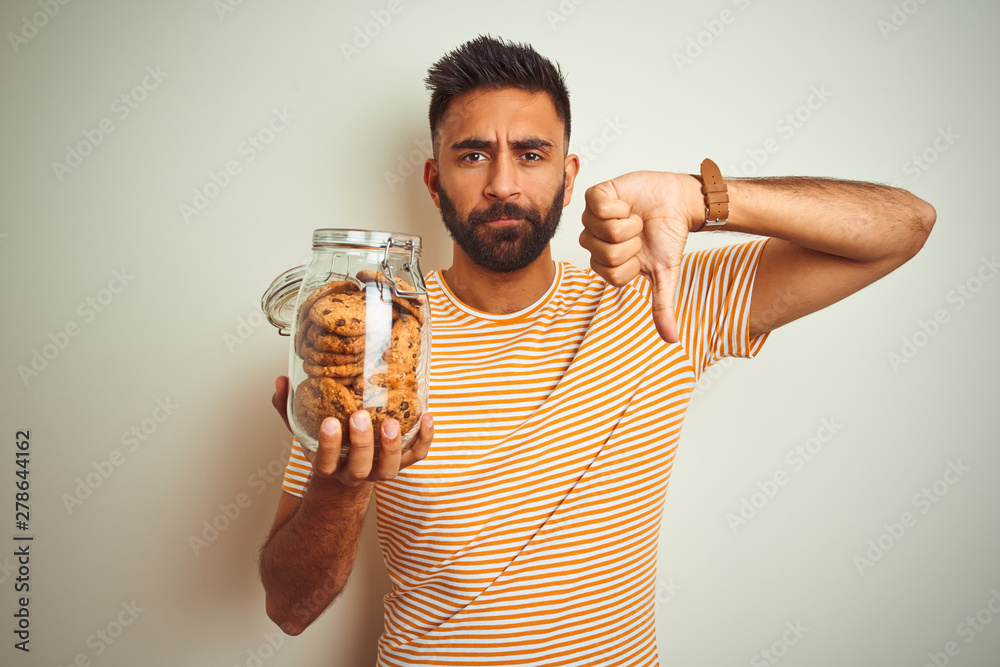 Young indian man holding jar of cookies standing over isolated white ...