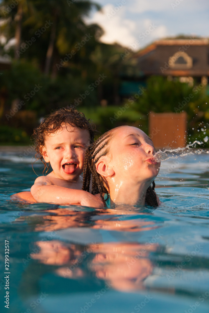 Little boy getting a piggyback ride from older girl while swimming in a ...