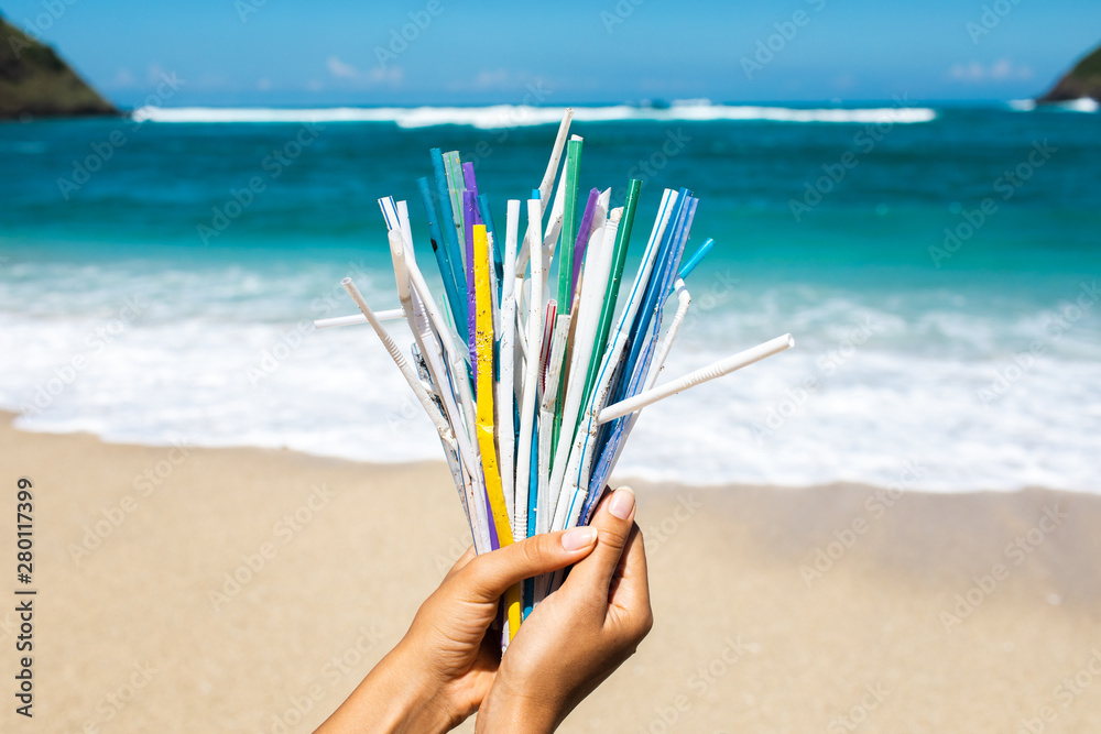 Hand holding heap of used plastic straws on background of clean beach ...