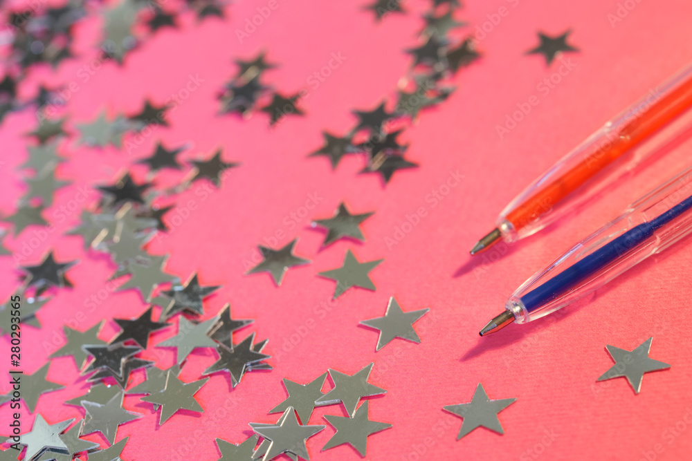 Blue and red fountain pens lie next to silver stars on a pink ...