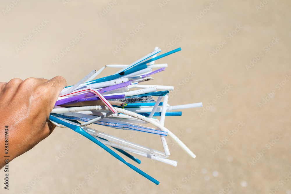 Hand holding heap of used plastic straws on background of clean beach ...