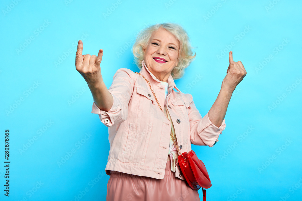 elder cheerful positive gorgeous lady making rock sign, isolated blue ...
