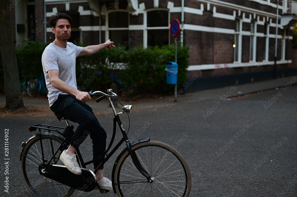 Dutch male student pointing to the left while riding on his bicycle ...