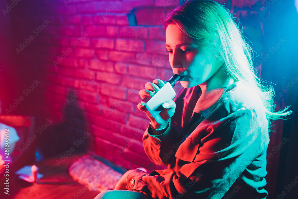 woman smokes a e-cigarette lying on the bed in the room. Smoker's ...