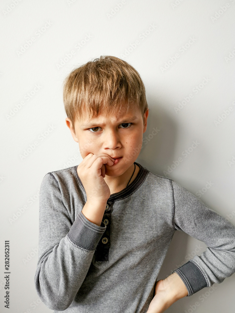 Thoughtful worried young boy biting his nails in trepidation as he ...