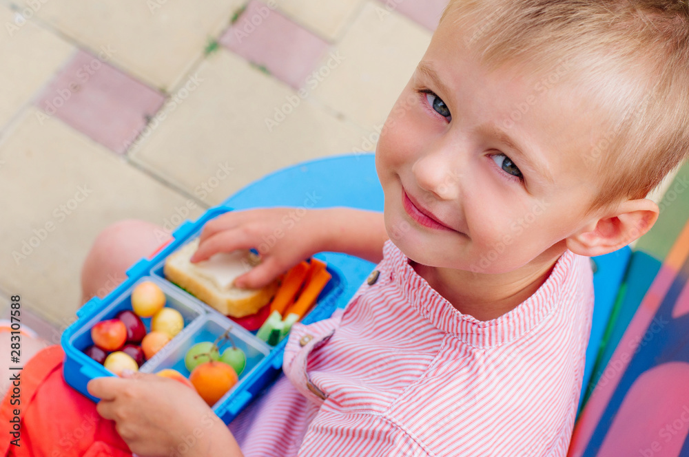 Smiling schoolboy eating his lunch from lunch box sitting outdoor Stock ...