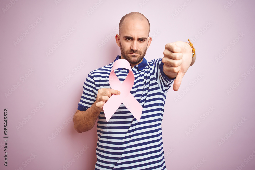 Young man holding pink brest cancer ribbon over isolated background ...