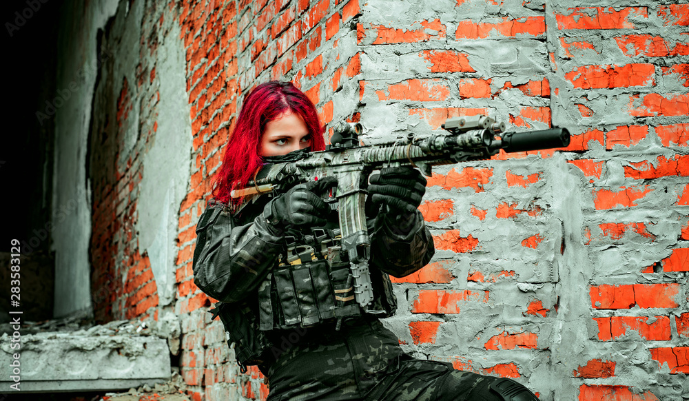 Airsoft red-hair woman in uniform with machine gun beside brick wall ...