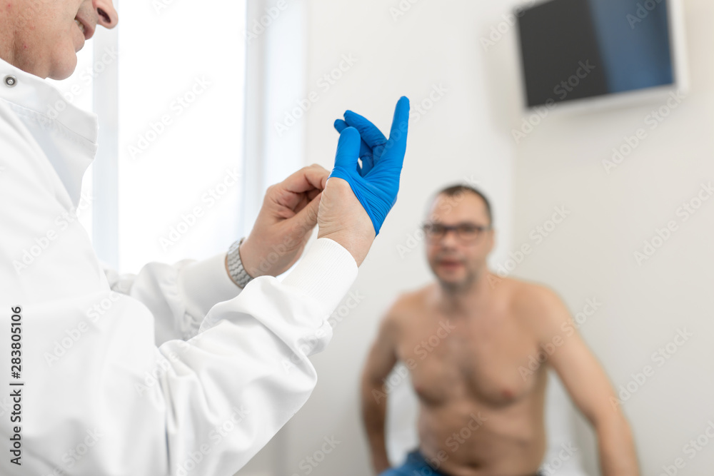 Doctor urologist puts a medical glove on the arm to examine the patient ...