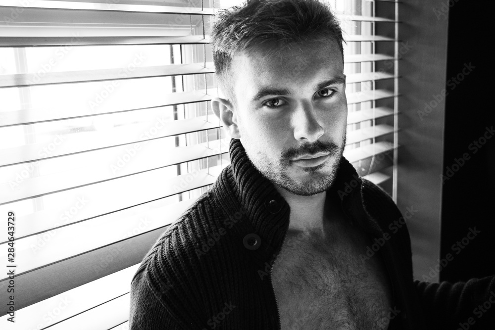Portrait of handsome man with beard standing next to window with open ...