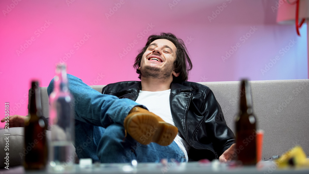 Relaxed drunk young man sitting on sofa, boozer enjoying music at dance ...
