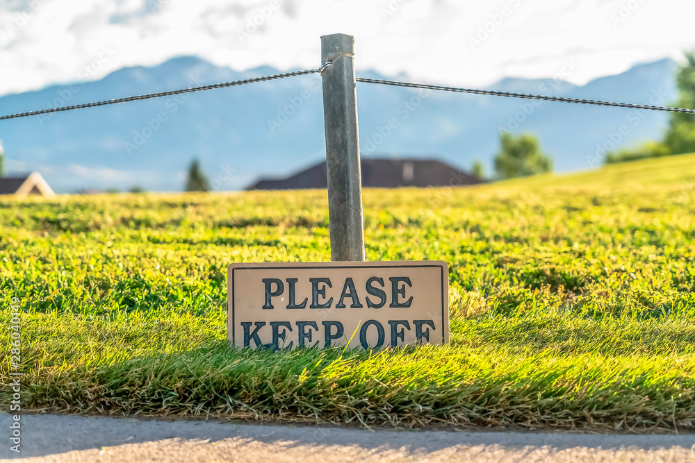 Please Keep Off sign against vibrant grasses and post of a wire fence ...
