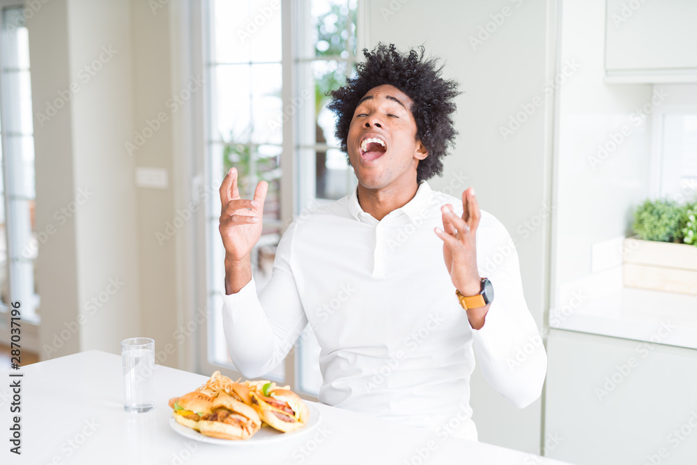 African American hungry man eating hamburger for lunch celebrating mad ...