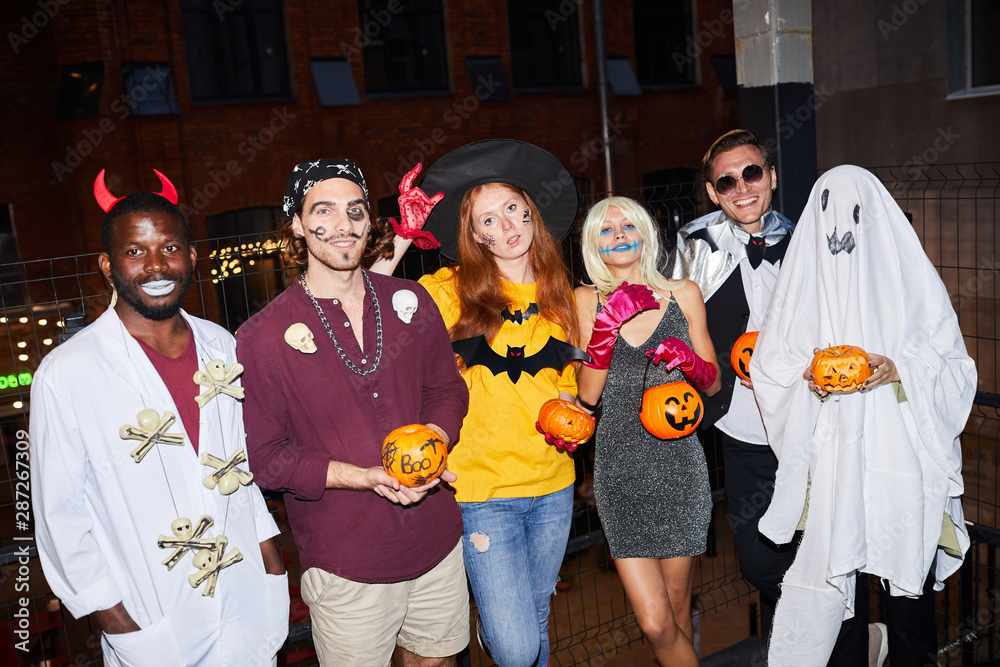 Group of young people wearing Halloween costumes posing during party in ...