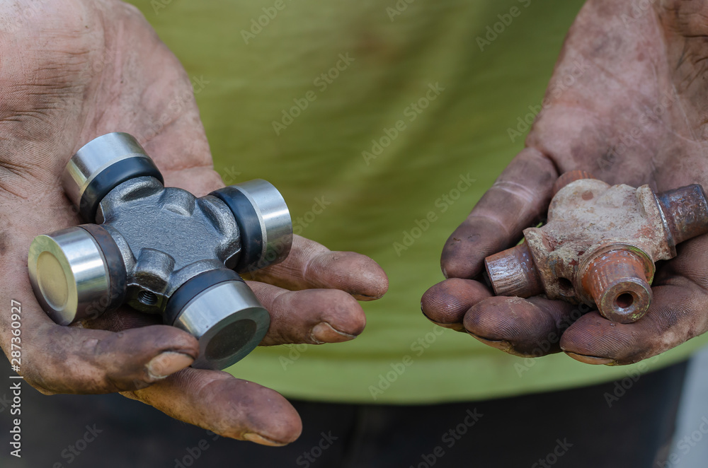 The car mechanic is holding in his hands an old with a new cross of the ...