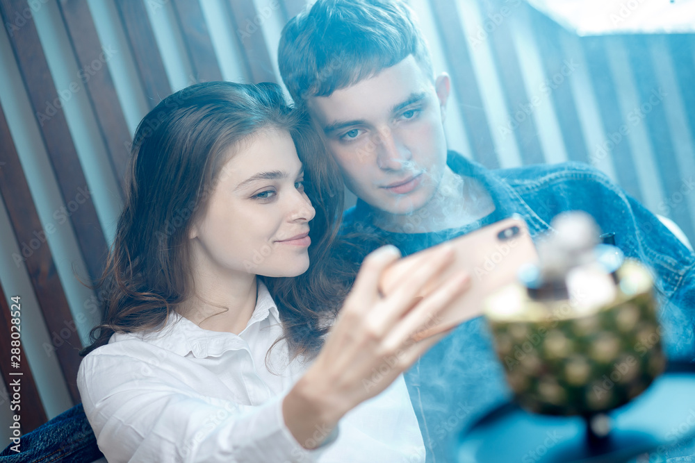 Beautiful young woman with guy hookah, blow smoke from tobacco and take ...