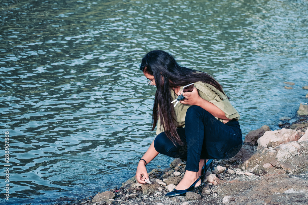 Indian girl with long hair throwing pebbles in water at lake. Nyari dam ...