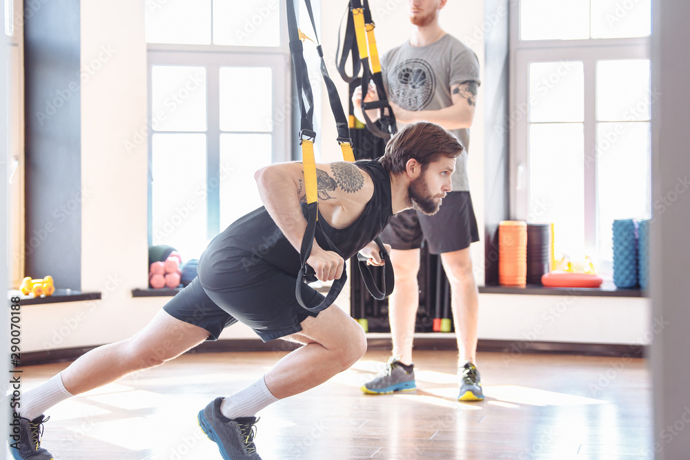 Positive young men athletes work out together in the gym using hanging ...